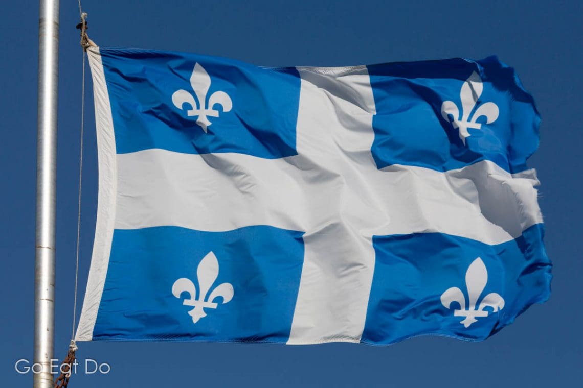 The blue and white Quebec flag bears four fleur-de-lys emblems and is ...